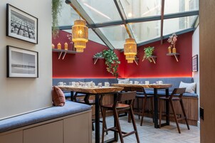 Interior moderno de café com teto de vidro, paredes vermelhas, móveis de madeira e luminárias pendentes.