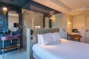 Quarto de hotel moderno com uma cama grande, banheiro com chuveiro e toucador com pia.