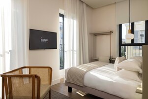 Quarto de hotel moderno com uma cama, televisão, cadeira e janela com cortinas.