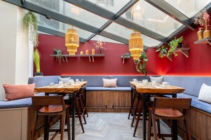 Restaurante com teto de vidro, mesas de madeira e assentos azuis.