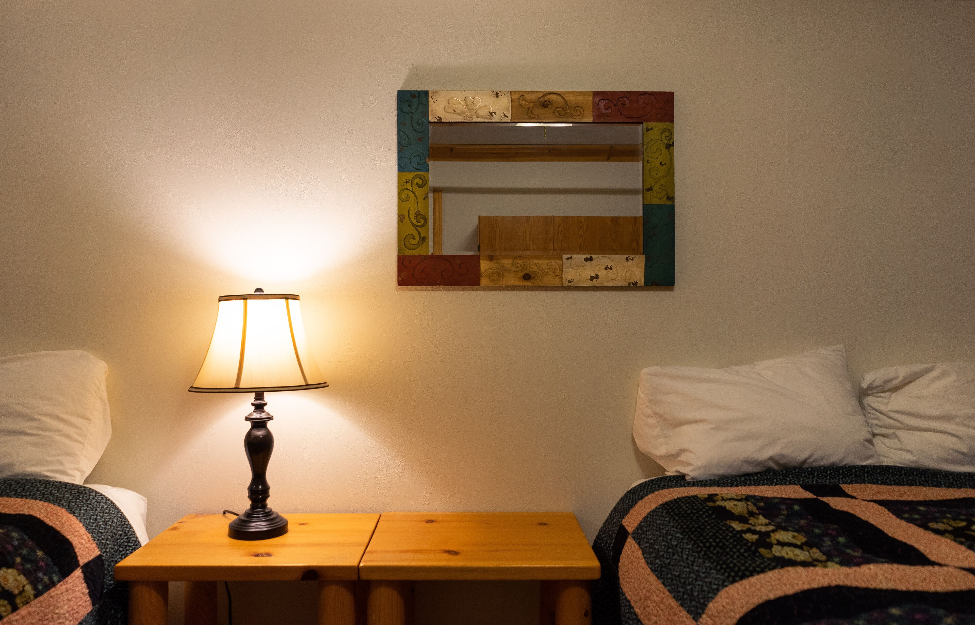 Quarto com duas camas, uma mesa de cabeceira com abajur e um espelho na parede.
