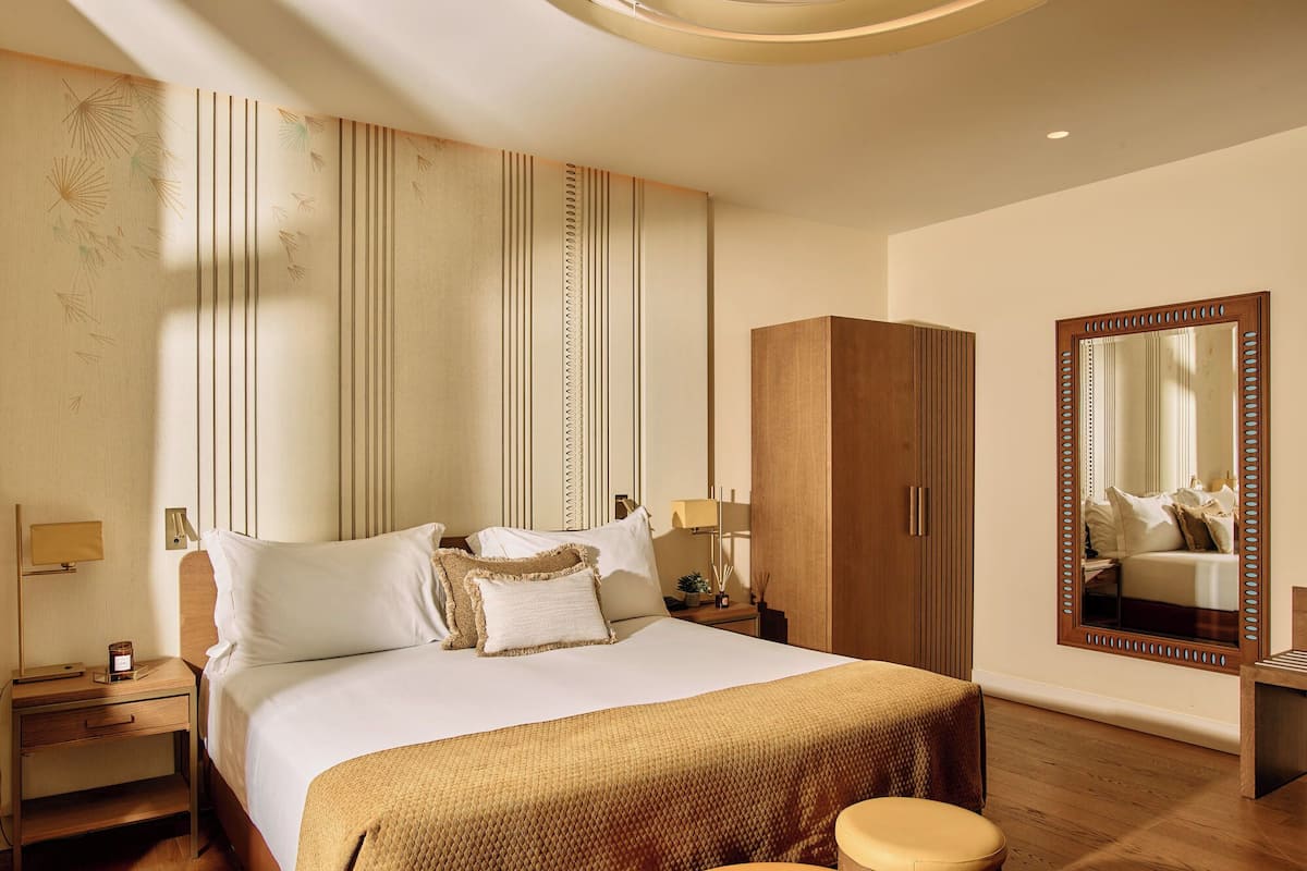 Quarto de hotel com uma cama grande, um guarda-roupa, um espelho e uma pequena mesa com abajur.