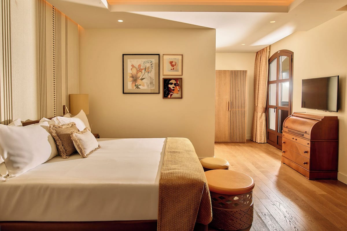 Quarto de hotel com uma cama grande, penteadeira de madeira, televisão e obras de arte na parede.
