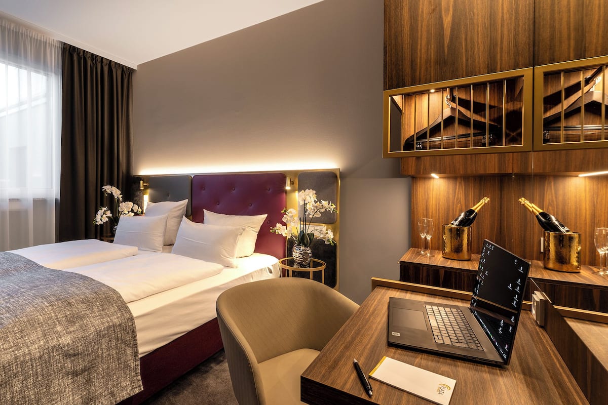 Quarto de hotel com uma cama grande, uma mesa com um laptop e um minibar.