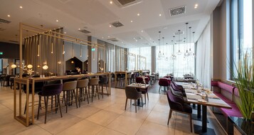 Um restaurante moderno com pé-direito alto, iluminação pendente e uma combinação de áreas de bar e refeições.