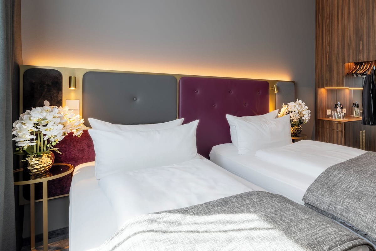 Quarto de hotel com duas camas, cabeceira de madeira, escrivaninha e espelho.