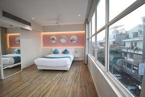Quarto moderno com uma cama grande, um espelho e vista da cidade através de grandes janelas.
