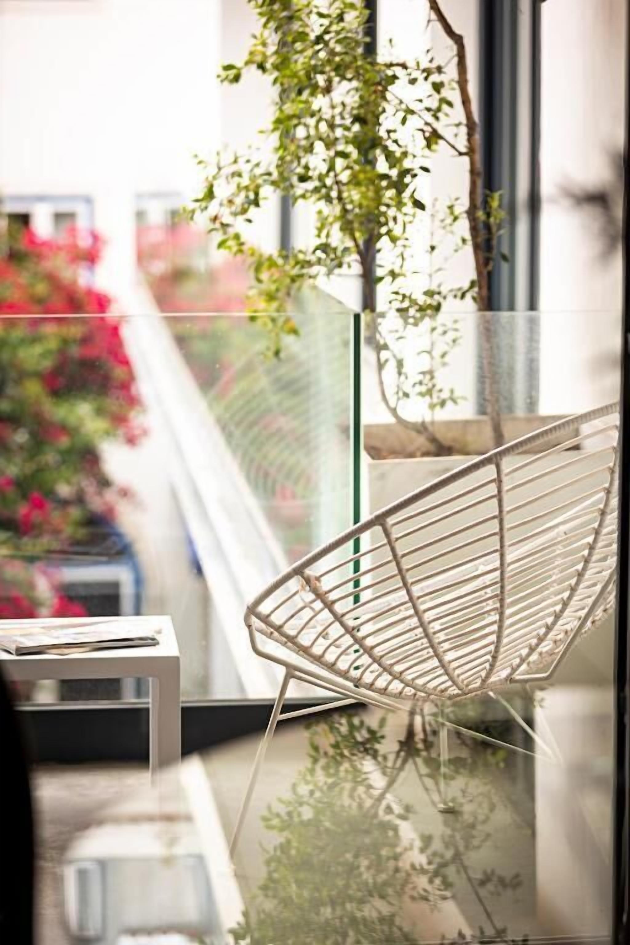 Interior moderno com uma cadeira branca, uma mesa de vidro e vista para uma varanda com plantas.