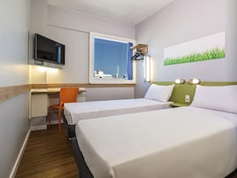 Quarto de hotel com duas camas, uma escrivaninha, uma cadeira, uma TV, uma janela com vista para a cidade e um quadro de grama.