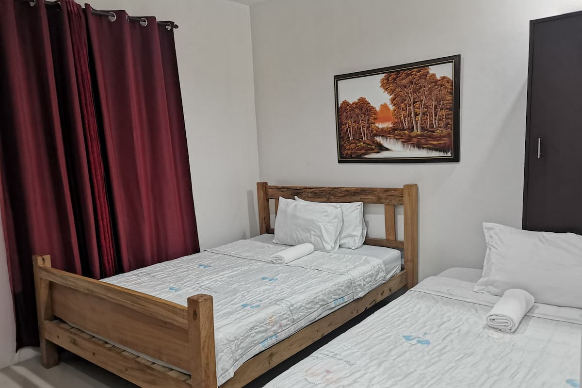 Uma cama de casal com estrutura de madeira e roupa de cama branca, uma cortina vermelha e um quadro de árvores na parede.