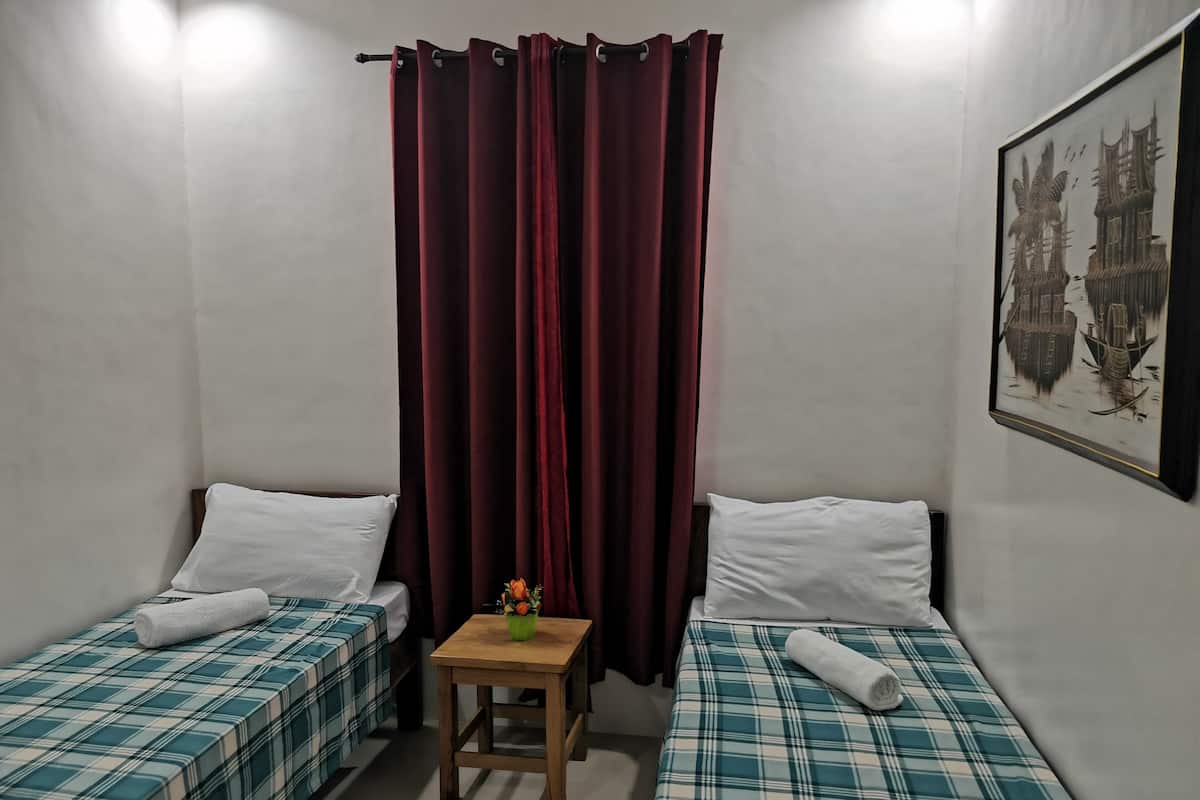 Quarto com duas camas, uma mesinha e uma cortina.