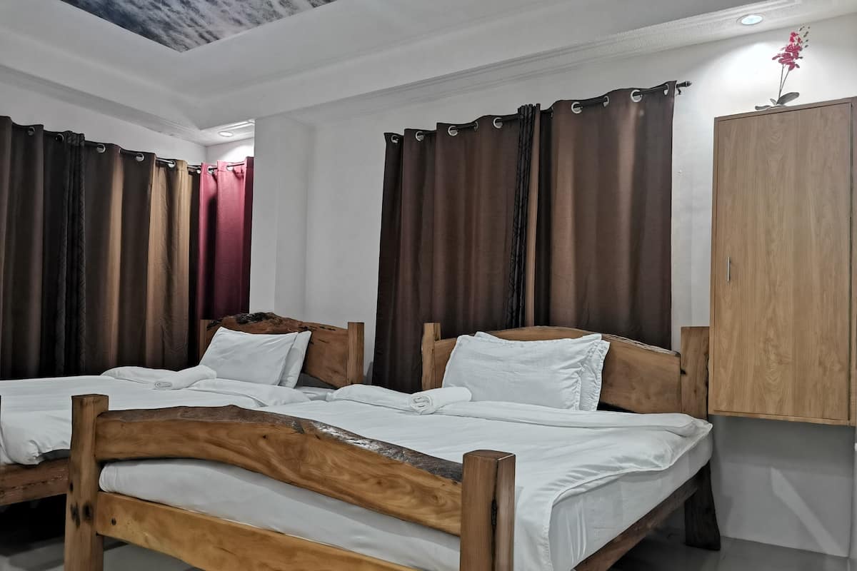 Quarto com duas camas de madeira, roupa de cama branca e cortinas escuras.