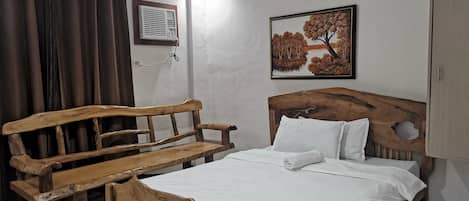 Quarto com cama de madeira, um banco de madeira, ar-condicionado fixado na parede e um quadro com árvores.
