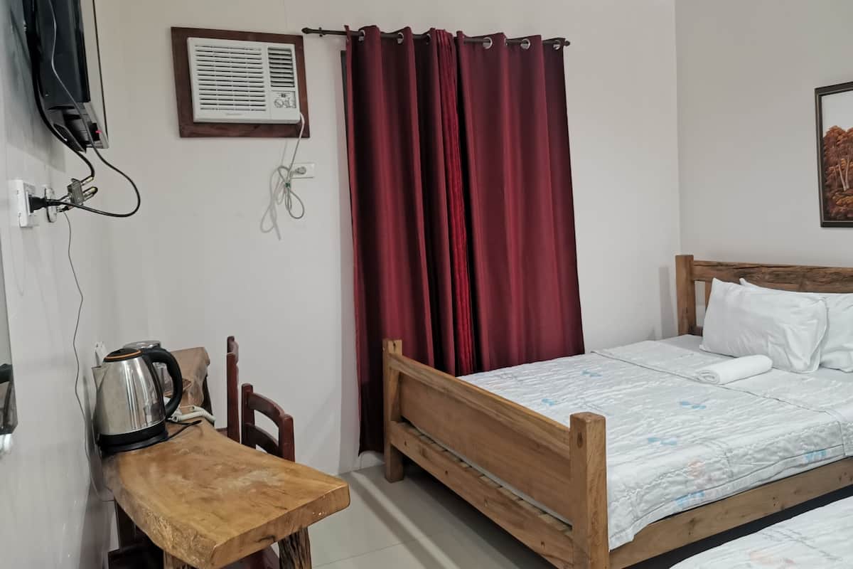 Quarto com cama de madeira, almofadas brancas, mesa de cabeceira de madeira com chaleira e cortina vermelha, além de ar-condicionado fixado na parede.