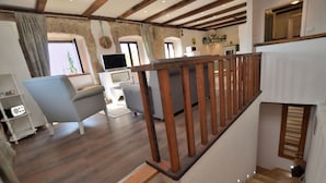Uma área de estar ampla com escada de madeira, um sofá cinza e uma televisão.