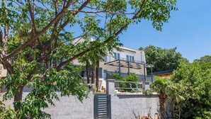 Uma casa moderna com varanda, rodeada por árvores e um muro branco.