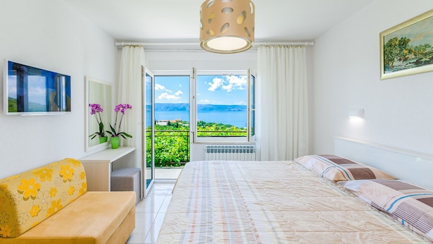 Quarto de hotel com cama, sofá, TV e vista para o mar.