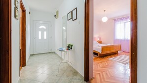 Corredor que dá para um quarto com cama, mesa de cabeceira e uma pequena mesa com uma planta.
