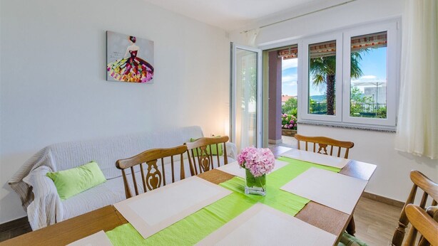 Uma sala de jantar com mesa posta para quatro pessoas, um sofá e um quadro na parede.