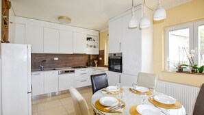 Cozinha moderna com armários brancos, uma mesa de jantar posta para quatro pessoas e uma janela com persianas.