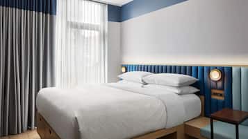 Quarto de hotel moderno com uma cama grande, uma mesinha de cabeceira e cabeceira com iluminação embutida.