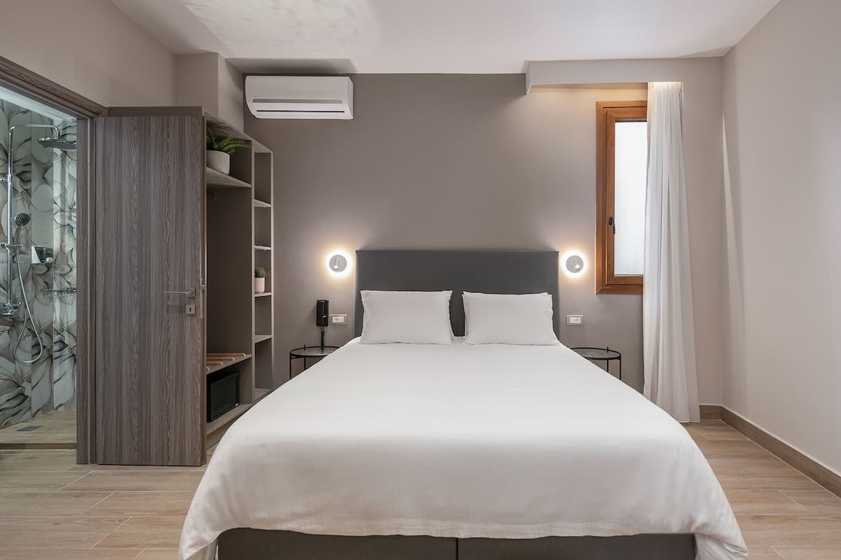 Um quarto moderno com uma cama grande, um guarda-roupa, uma mesa pequena com abajur e uma janela com cortinas.