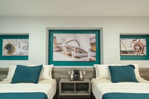 Quarto de hotel com duas camas, uma mesinha de cabeceira de madeira e três quadros na parede.