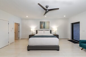 Quarto moderno com uma cama grande, duas mesas de cabeceira com abajures, um ventilador de teto e uma janela ampla.