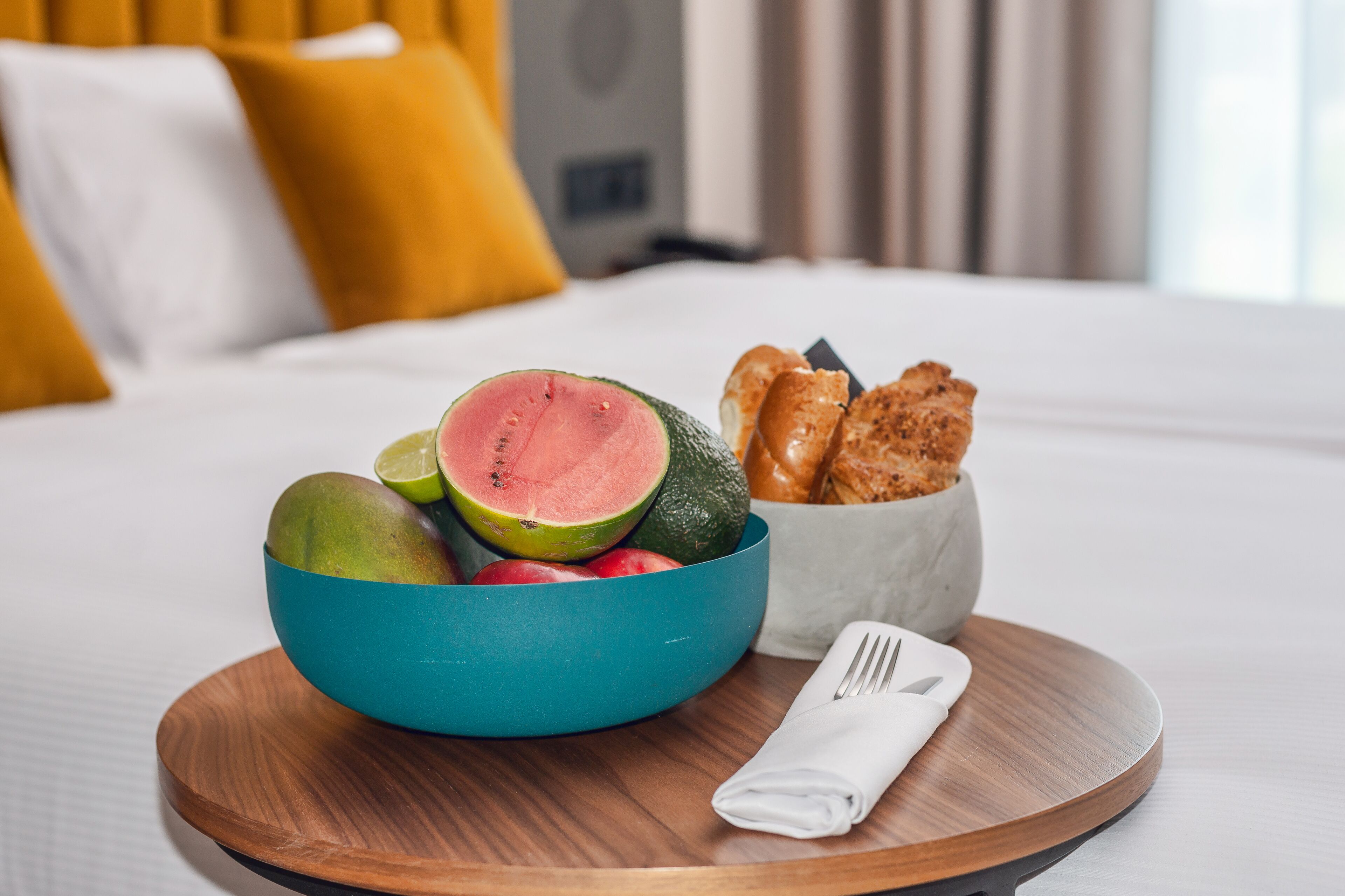 Bandeja de café da manhã com uma tigela de frutas e pão sobre uma mesa de madeira em um quarto de hotel.