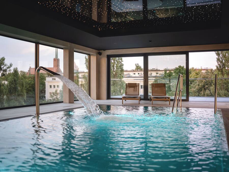 Piscina interna com água cristalina, uma fonte e espreguiçadeiras.