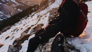 Uma pessoa sentada em uma rocha com uma mochila vermelha, admirando uma paisagem montanhosa coberta de neve.