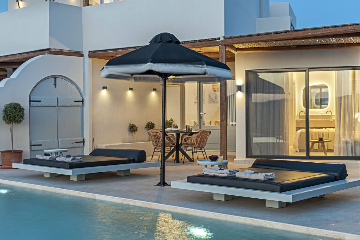 Uma área na beira da piscina com duas espreguiçadeiras, uma mesa e um guarda-sol.