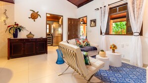 Uma sala de estar ampla com um sofá branco, um tapete azul estampado e teto de madeira.
