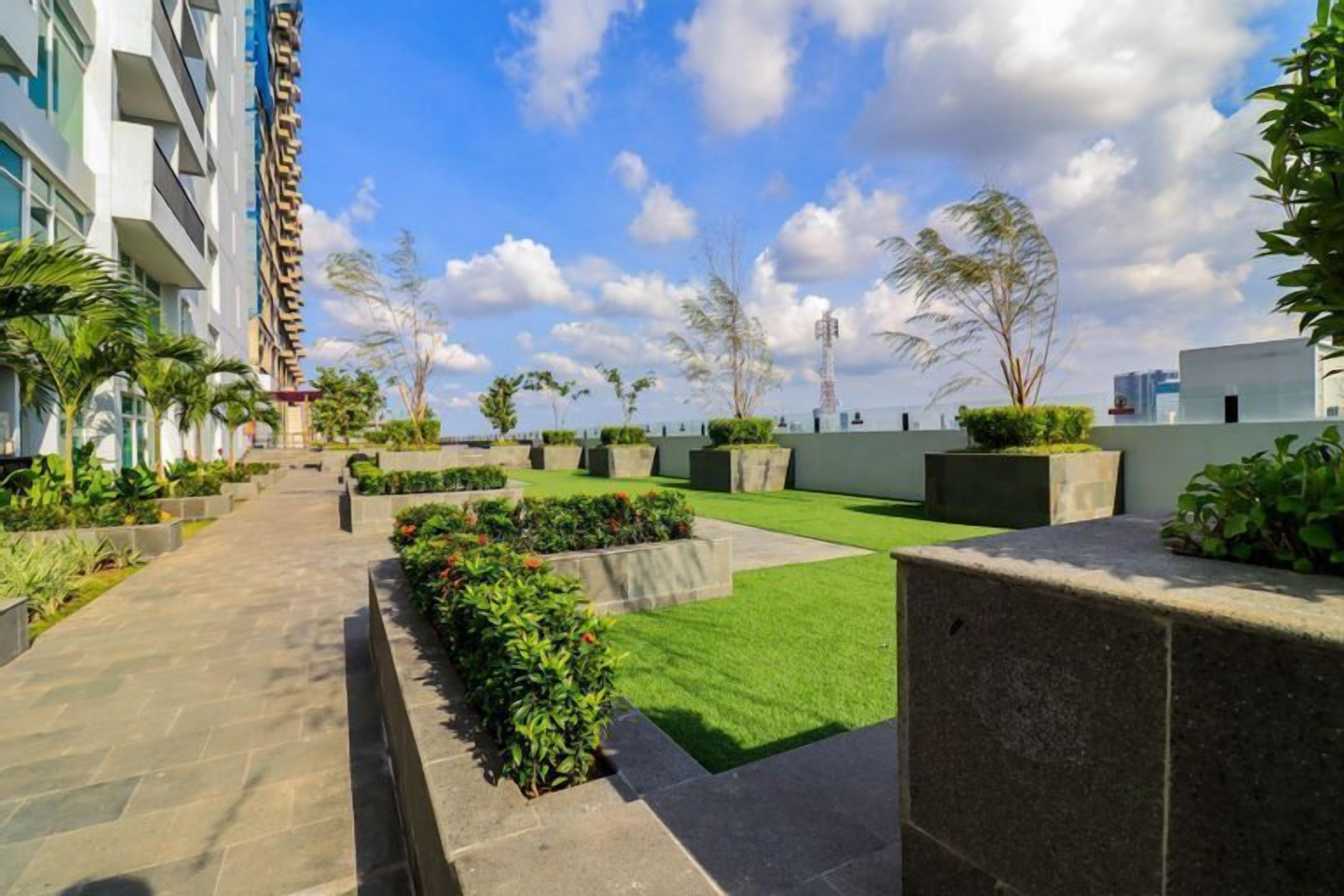 Pátio moderno de hotel com calçada pavimentada, gramados verdes e diversas plantas.