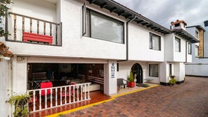 Um edifício de dois andares com área de estar coberta ao ar livre, varanda com mobiliário vermelho e um pátio com piso de tijolos.