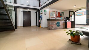 Um saguão de hotel com balcão de recepção, escada e um vaso de planta.