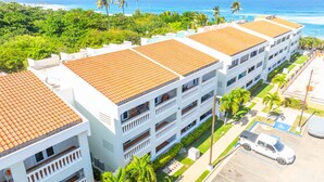 Um hotel com vários andares, telhado em telhas vermelhas, varandas e um estacionamento com um carro branco.