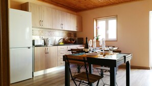 Uma cozinha com armários de madeira, geladeira, mesa de jantar com cadeiras e uma janela com luz natural.