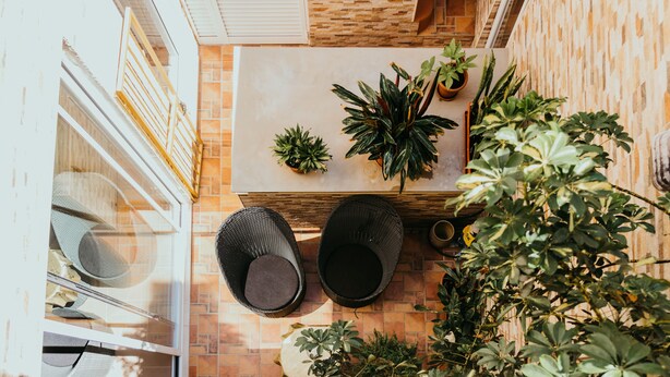 Um pátio externo com uma mesa, duas cadeiras de vime e várias plantas em vasos.