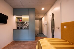 Quarto de hotel compacto com cama, cozinha compacta, área de chuveiro e banheiro.