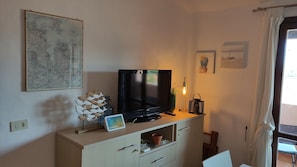 Uma sala de estar com televisão sobre um armário de madeira, um mapa na parede e uma janela com cortinas.
