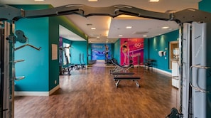 Academia com equipamentos de exercício, piso de madeira e paredes cor de verde-água.