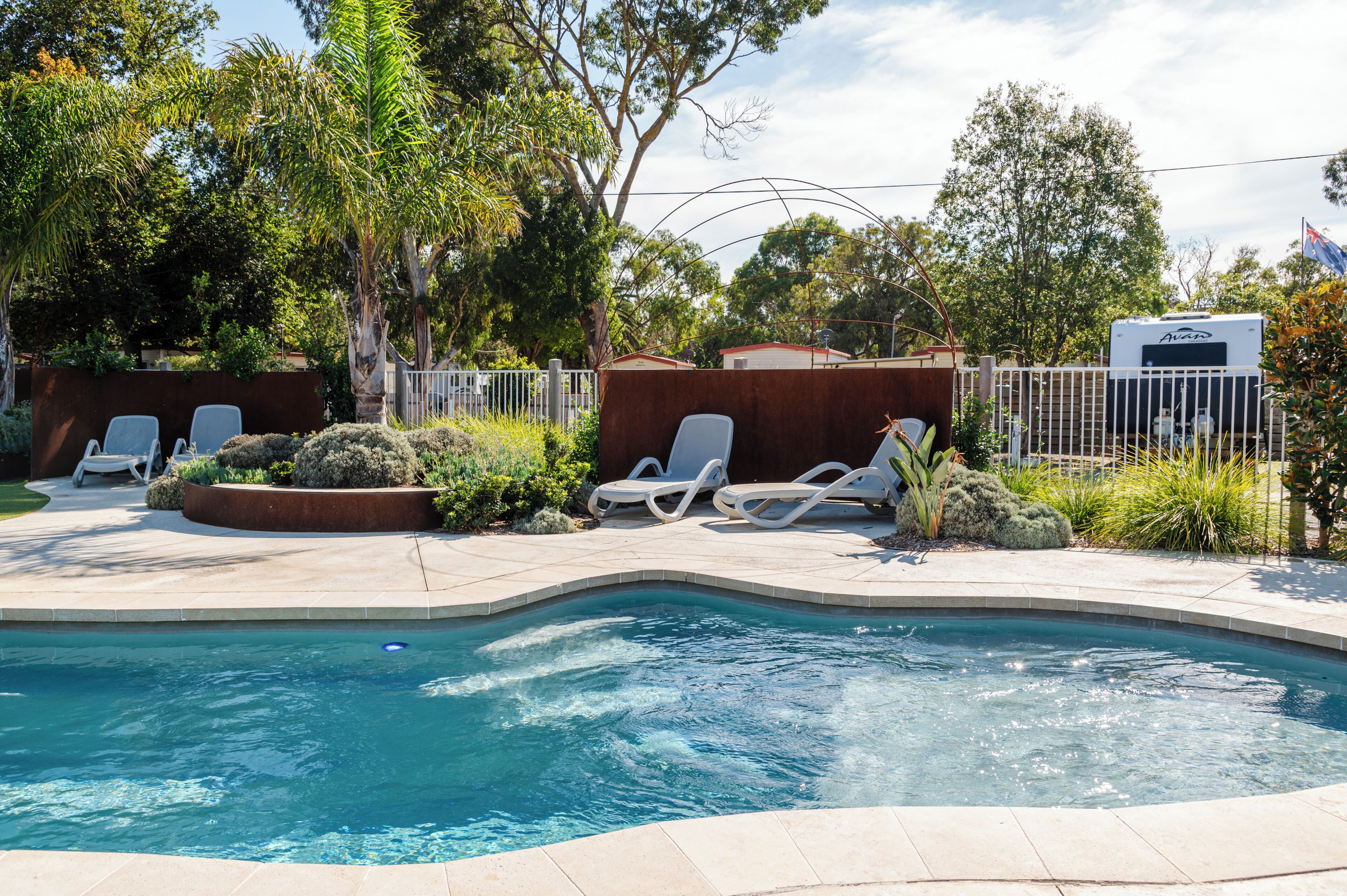 Piscina com espreguiçadeiras e área cercada com vegetação.