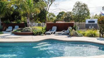 Piscina com espreguiçadeiras e área cercada com vegetação.