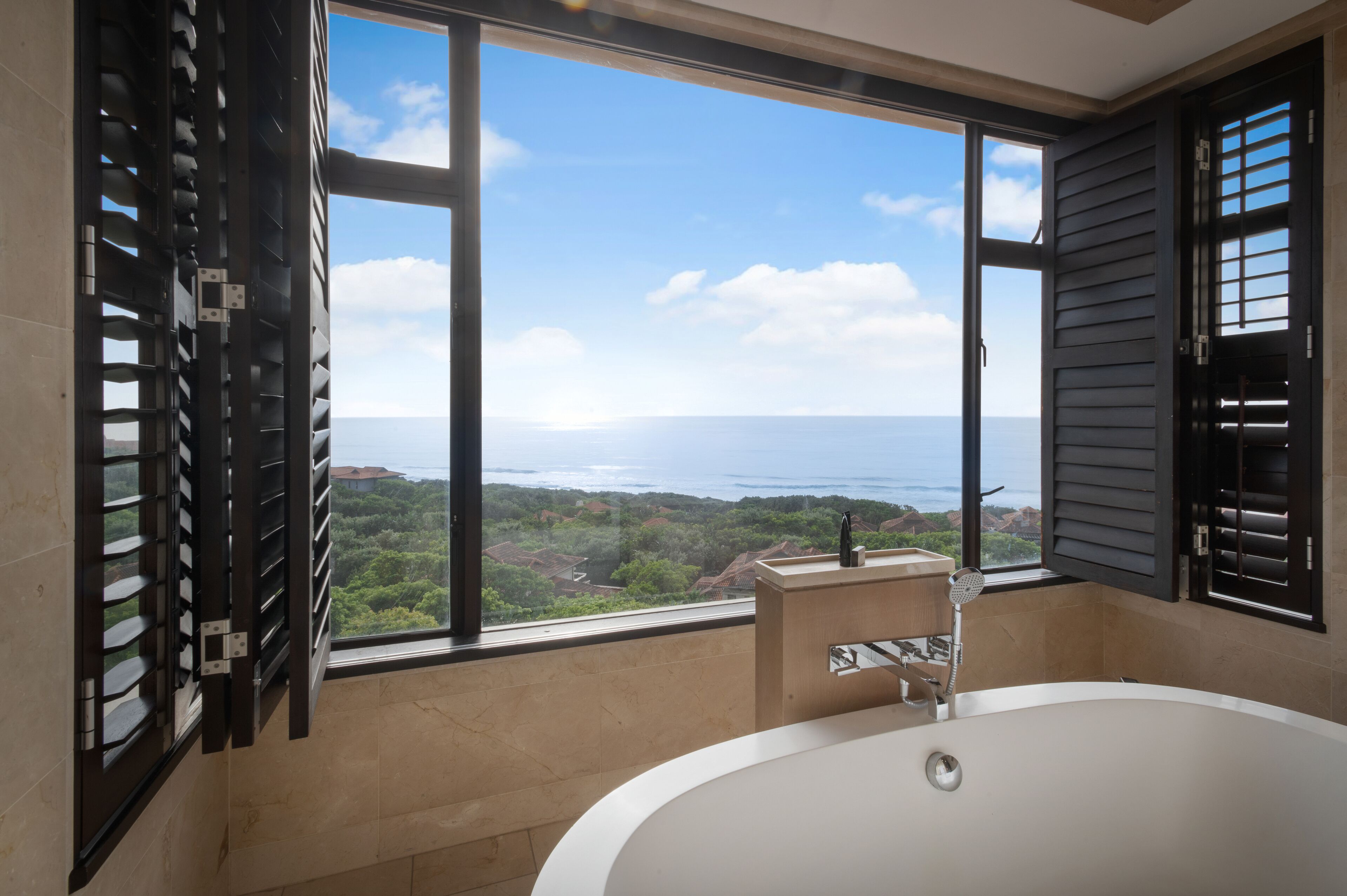 Uma casa de banho moderna com uma banheira grande, vista para o oceano e uma janela com persianas.