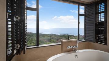 Uma casa de banho moderna com uma banheira grande, vista para o oceano e uma janela com persianas.