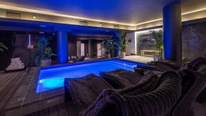 Uma área interna de piscina moderna com iluminação azul, cadeiras de descanso e plantas em vasos.