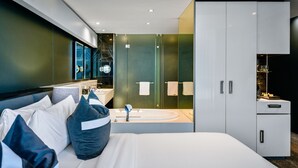 Quarto de hotel moderno com uma cama grande, banheiro com banheira e um guarda-roupa.