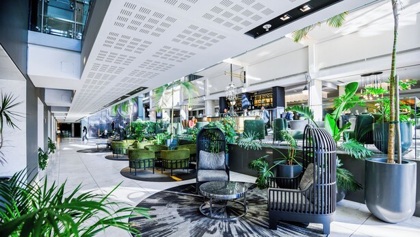 Um lobby moderno com áreas de estar, um bar e plantas dentro de casa.