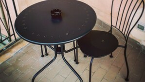 Mesa redonda com estrutura de metal preto e um pequeno objeto preto sobre ela, rodeada por duas cadeiras de metal preto.